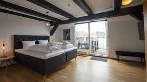 Quarto moderno com cama grande, mesinha de cabeceira pequena, um banco e porta de vidro deslizante para área externa.