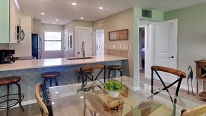 Uma cozinha moderna com ilha central, banquetas e mesa de jantar com cadeiras.