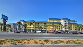 Um hotel com vários andares, um teto azul e um estacionamento com diversos carros.