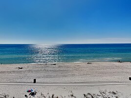 Uma praia com céu claro, mar calmo e algumas pessoas e guarda-sóis.