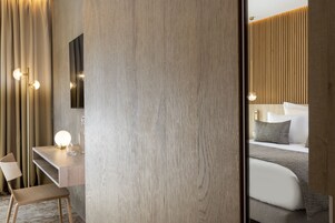 Quarto de hotel moderno com escrivaninha de madeira, uma cadeira, cama com roupa de cama branca e painel de parede em madeira.