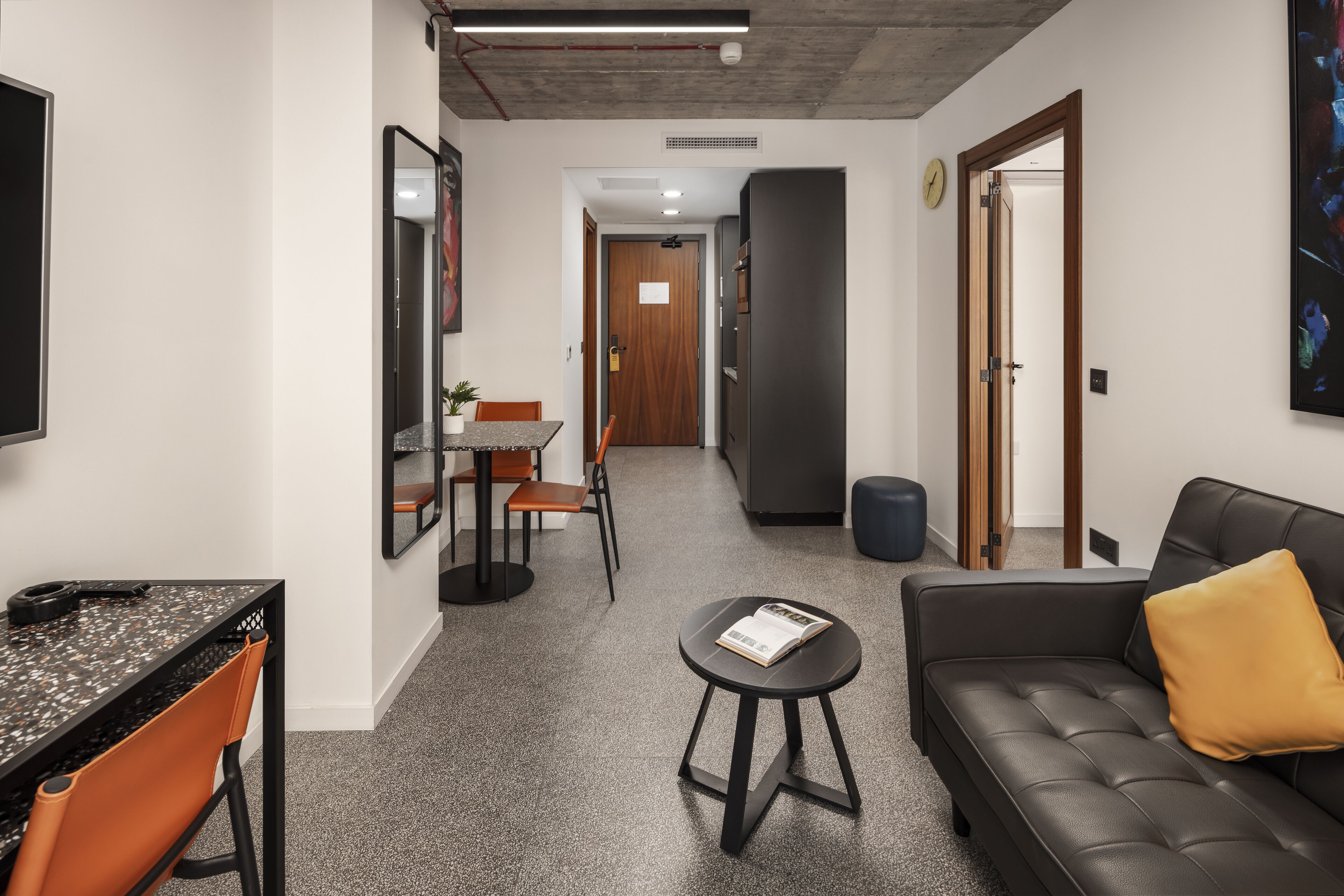 Uma sala de estar moderna com um sofá de couro preto, uma mesinha redonda e uma área de jantar com mesa e cadeiras.