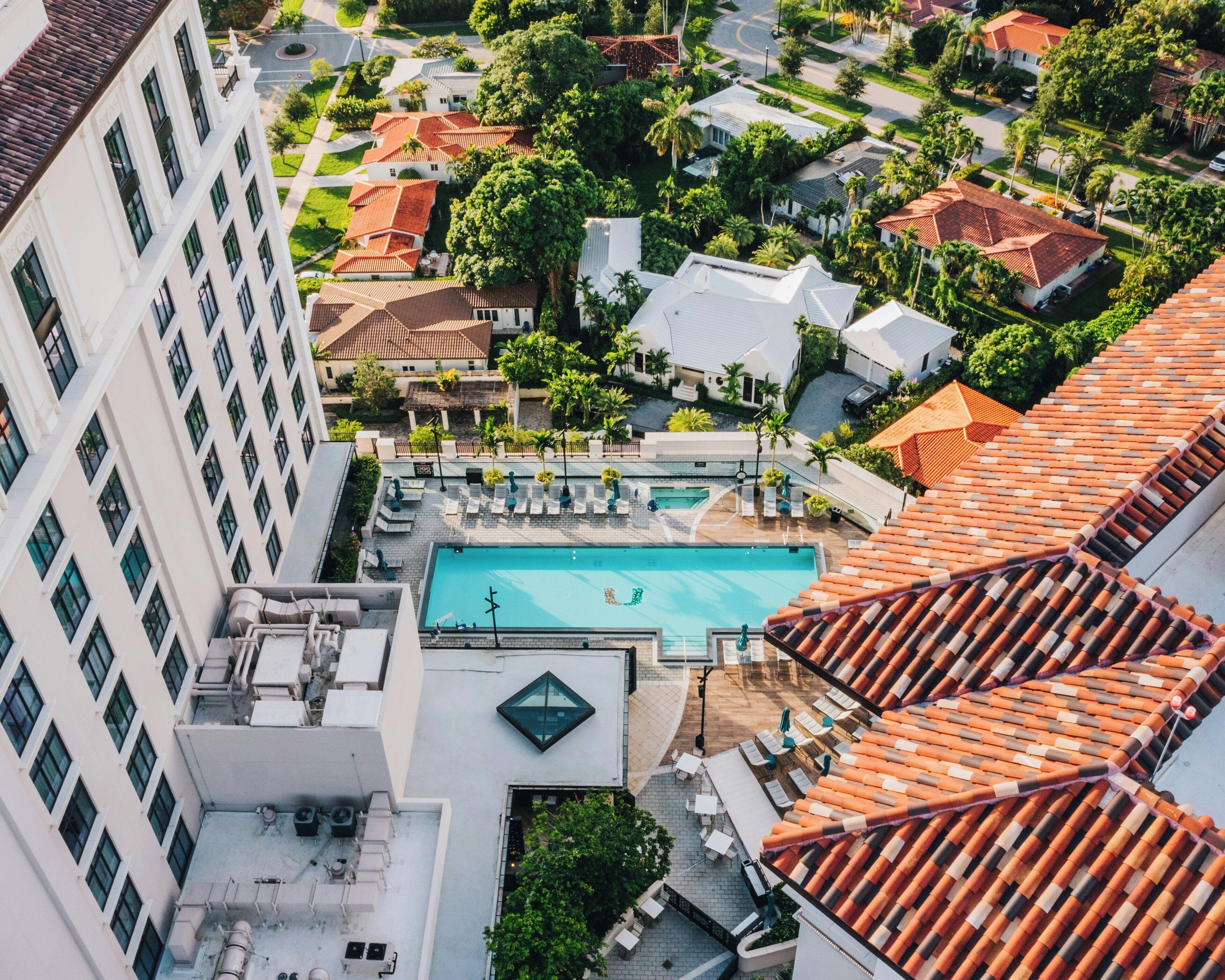 Um hotel moderno com piscina no terraço, diversas varandas e paisagem verde exuberante.