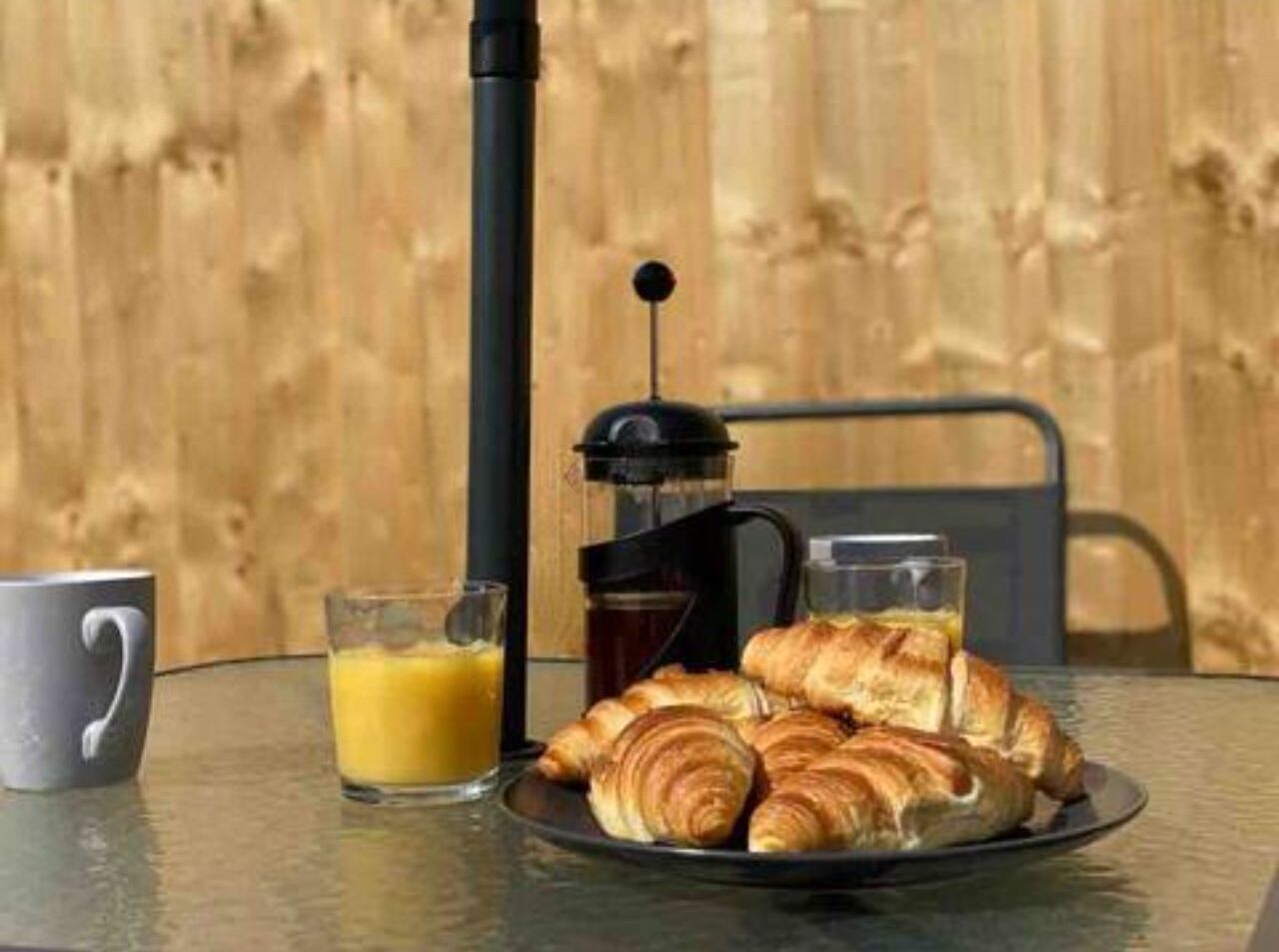 Uma mesa com uma cafeteira, um prato de croissants, um copo de suco de laranja e uma caneca.