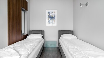 Quarto moderno com duas camas de solteiro, um guarda-roupa de madeira, uma mesinha e luminária fixada na parede.