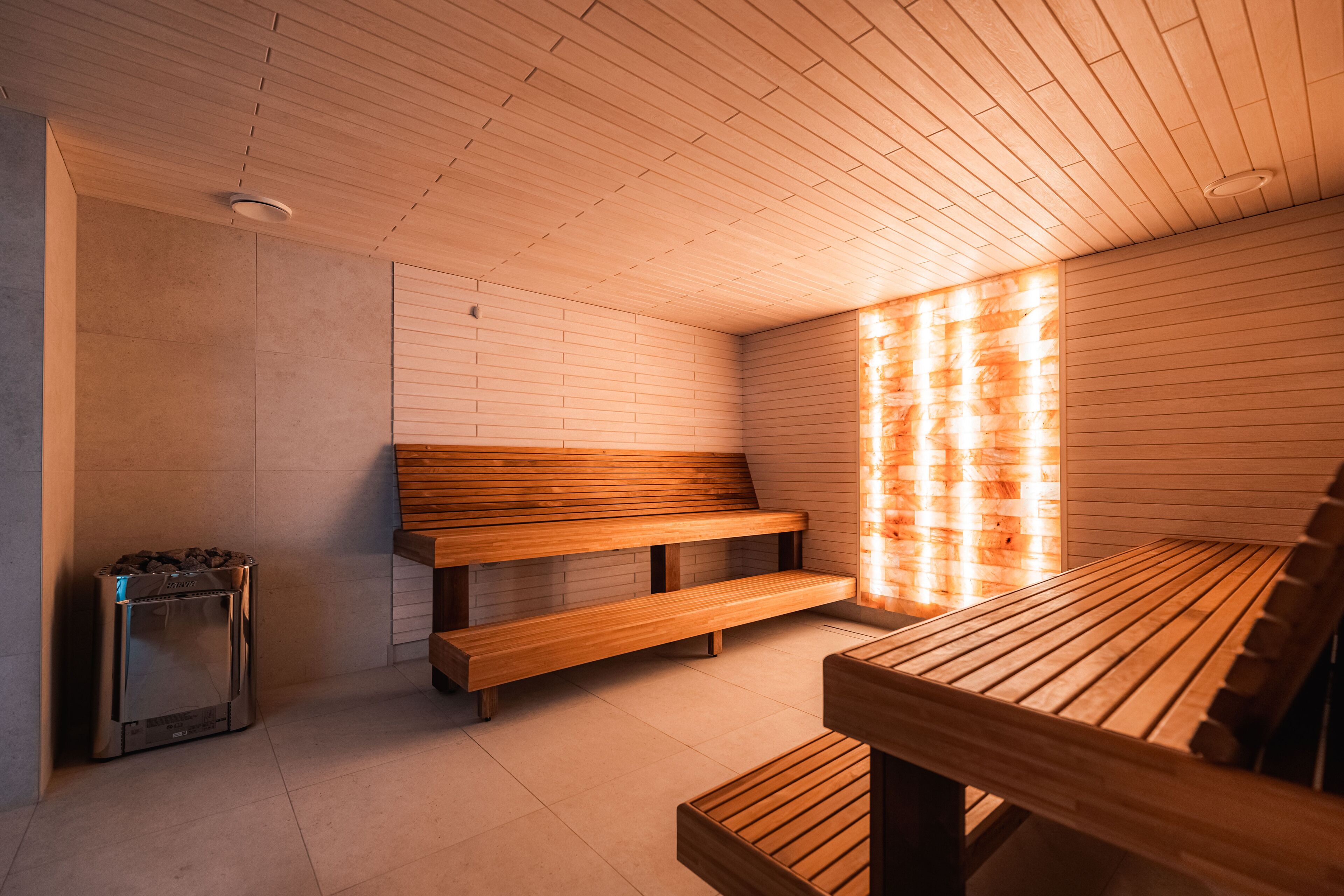 Uma sala de sauna com bancos de madeira e um assento de banco, um aquecedor de sauna e uma janela com design em ripas de madeira.