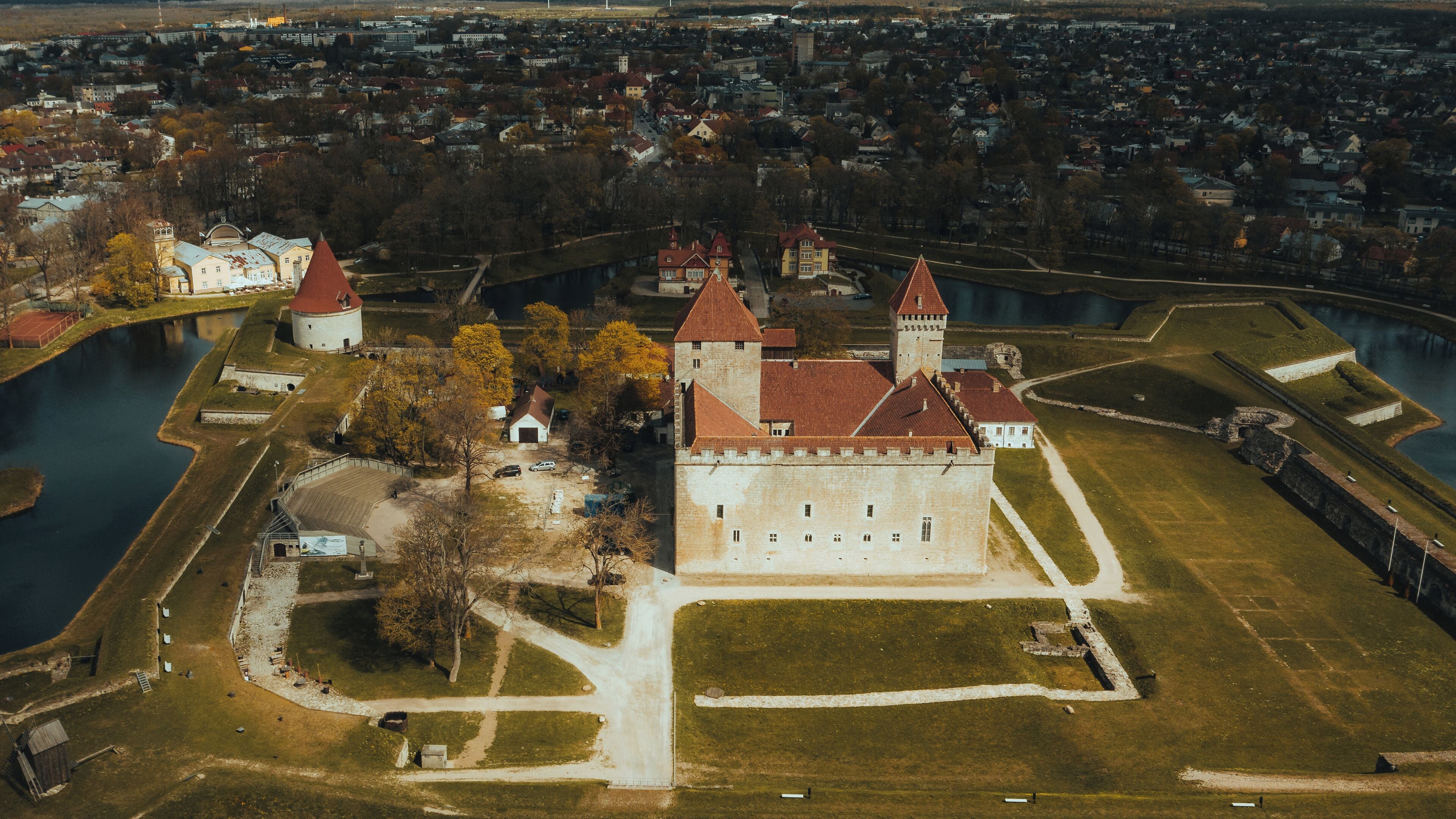 Vista aérea de um castelo histórico com fosso, rodeado por um parque e um rio.