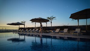 Uma piscina com espreguiçadeiras e guarda-sóis, cercada por palmeiras.