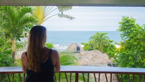 Uma mulher observa uma praia tropical com palmeiras e um bangalô de palha.
