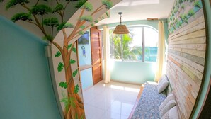 Quarto com um mural de árvore, um banco de madeira com almofadas, uma televisão e uma janela com vista para palmeiras.