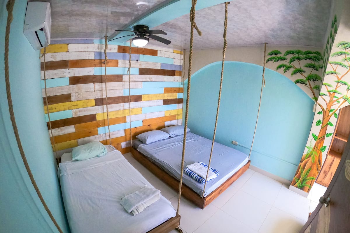 Quarto com teto inclinado, cama com estrutura de madeira, balanço pendurado e parede com design de painel de madeira colorido.
