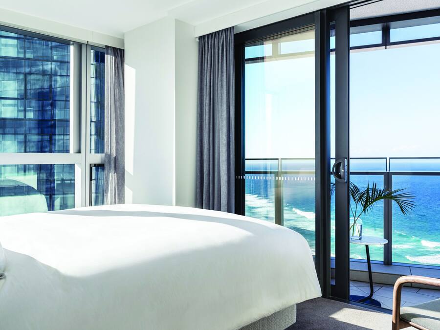 Quarto de hotel com uma cama grande, varanda e vista para o oceano, e decoração moderna.