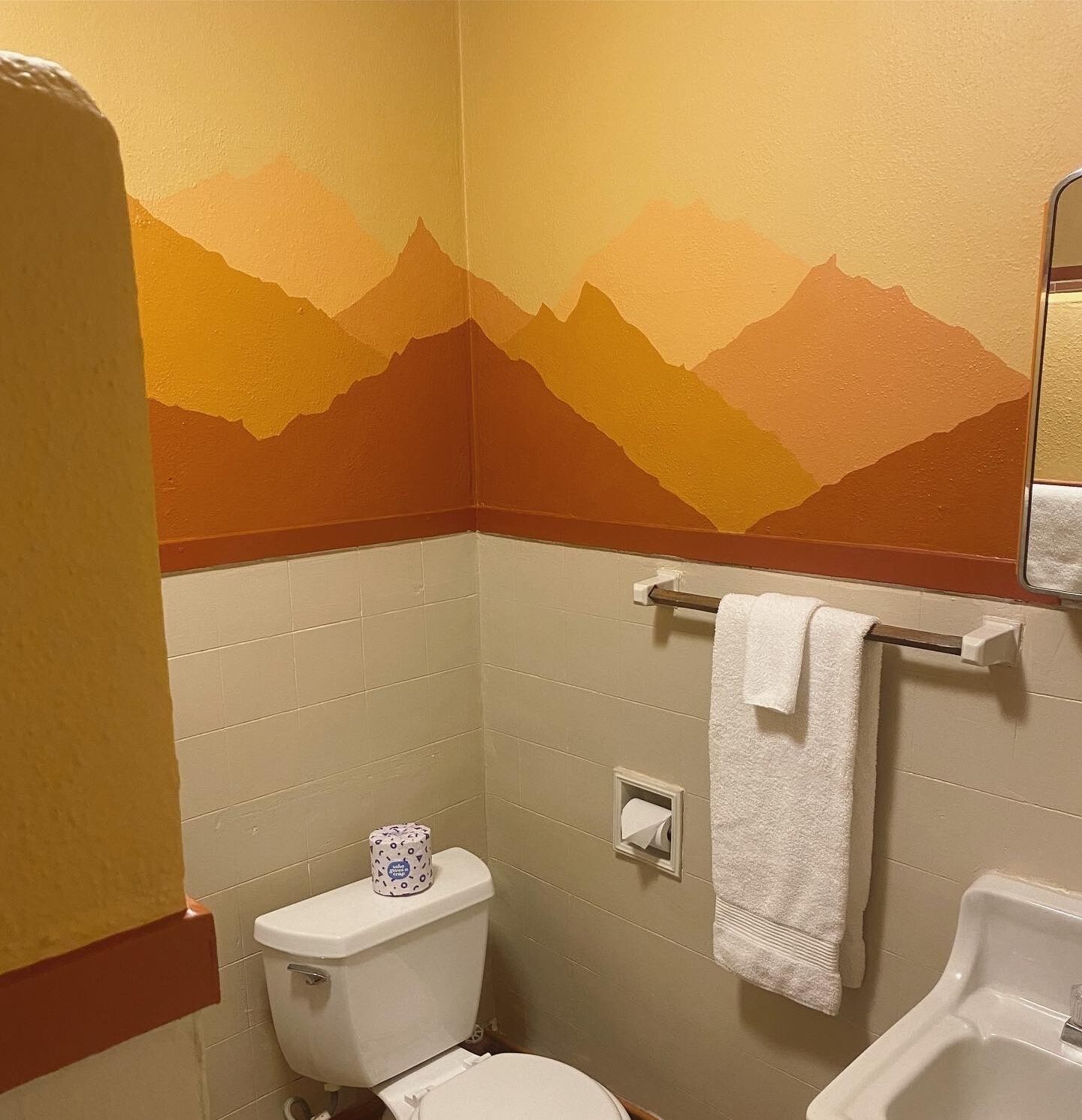 Casa de banho com um mural temático de montanha, sanita, bidé e suporte para toalhas.