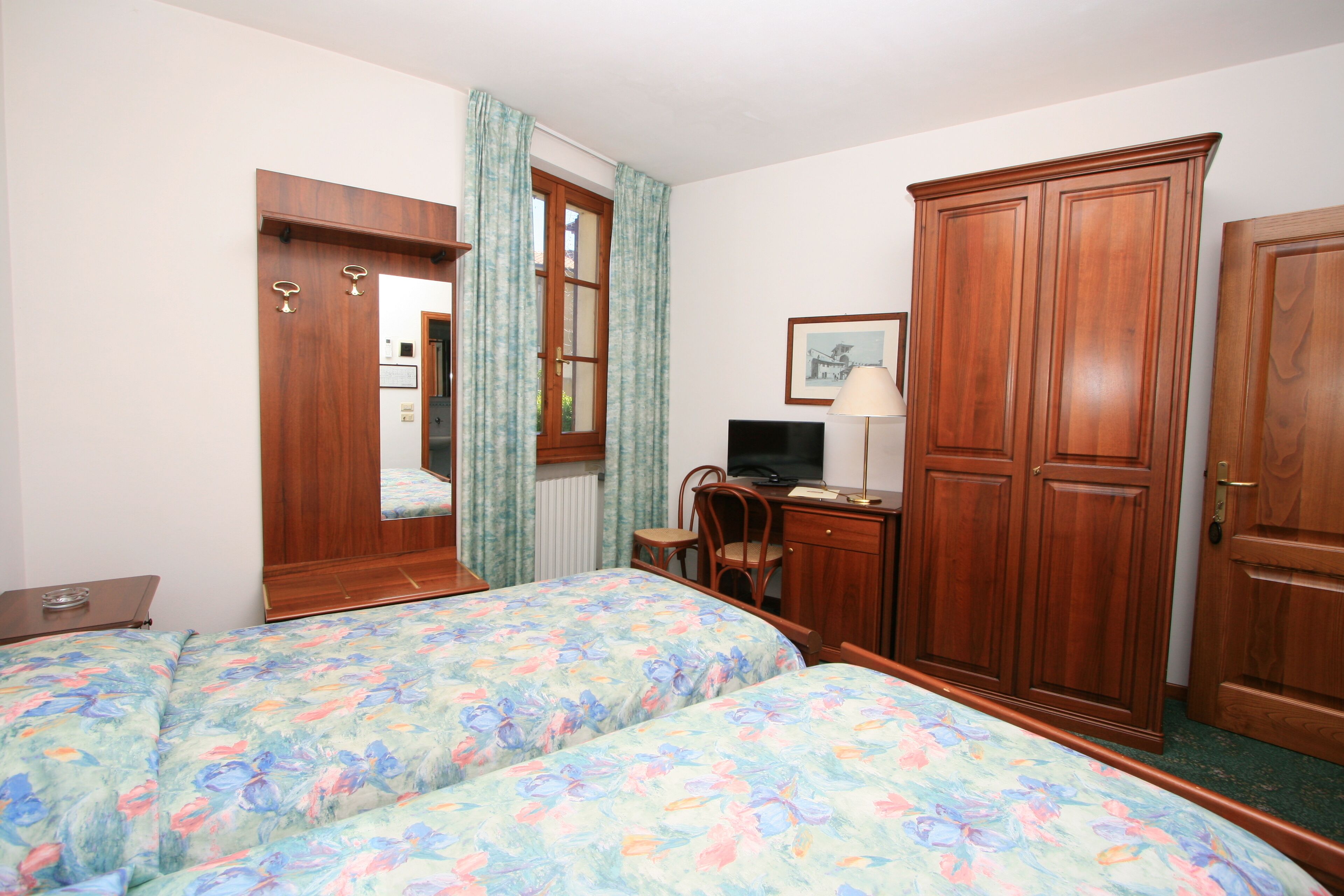 Quarto com duas camas, uma escrivaninha, uma cadeira, uma televisão e armários de madeira.