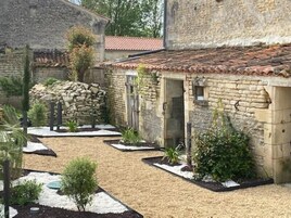 Um edifício de pedra com telhado de telhas, uma parede de pedra e um jardim com plantas e um caminho.