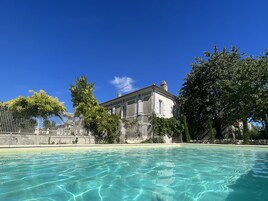 Uma piscina cristalina com um edifício ao fundo.