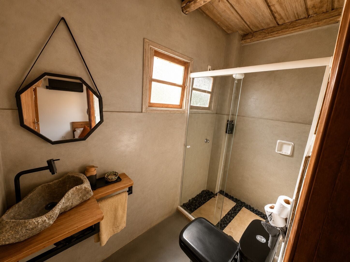 Uma casa de banho com toucador de madeira, espelho, chuveiro com portas de vidro e janela.