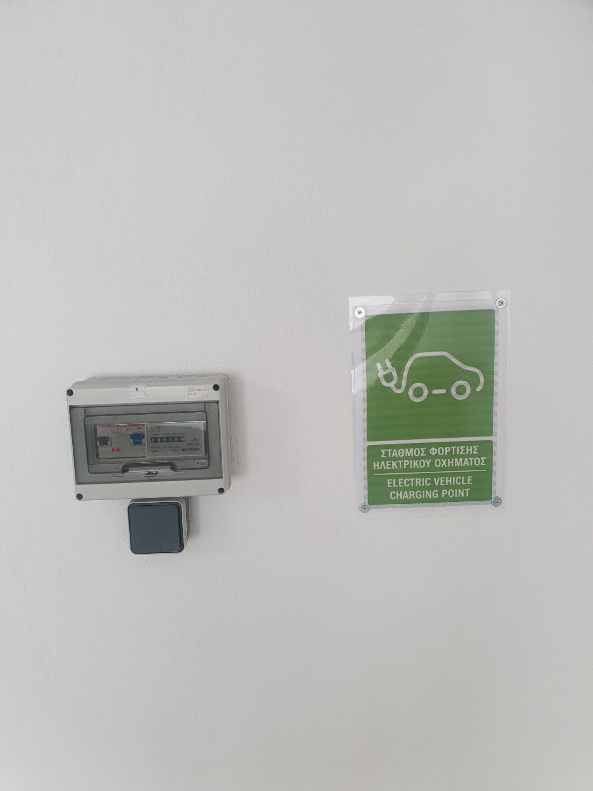 Estação de carregamento para veículos elétricos, com sinalização em grego e inglês.