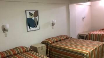 Quarto de hotel com três camas, cada uma com roupa de cama listrada, uma pequena mesa de cabeceira, uma luminária na parede e um quadro emoldurado.