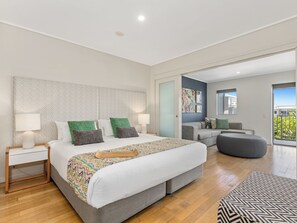 Quarto moderno com cama grande, mesas de cabeceira, sofá cinza e varanda com vista.