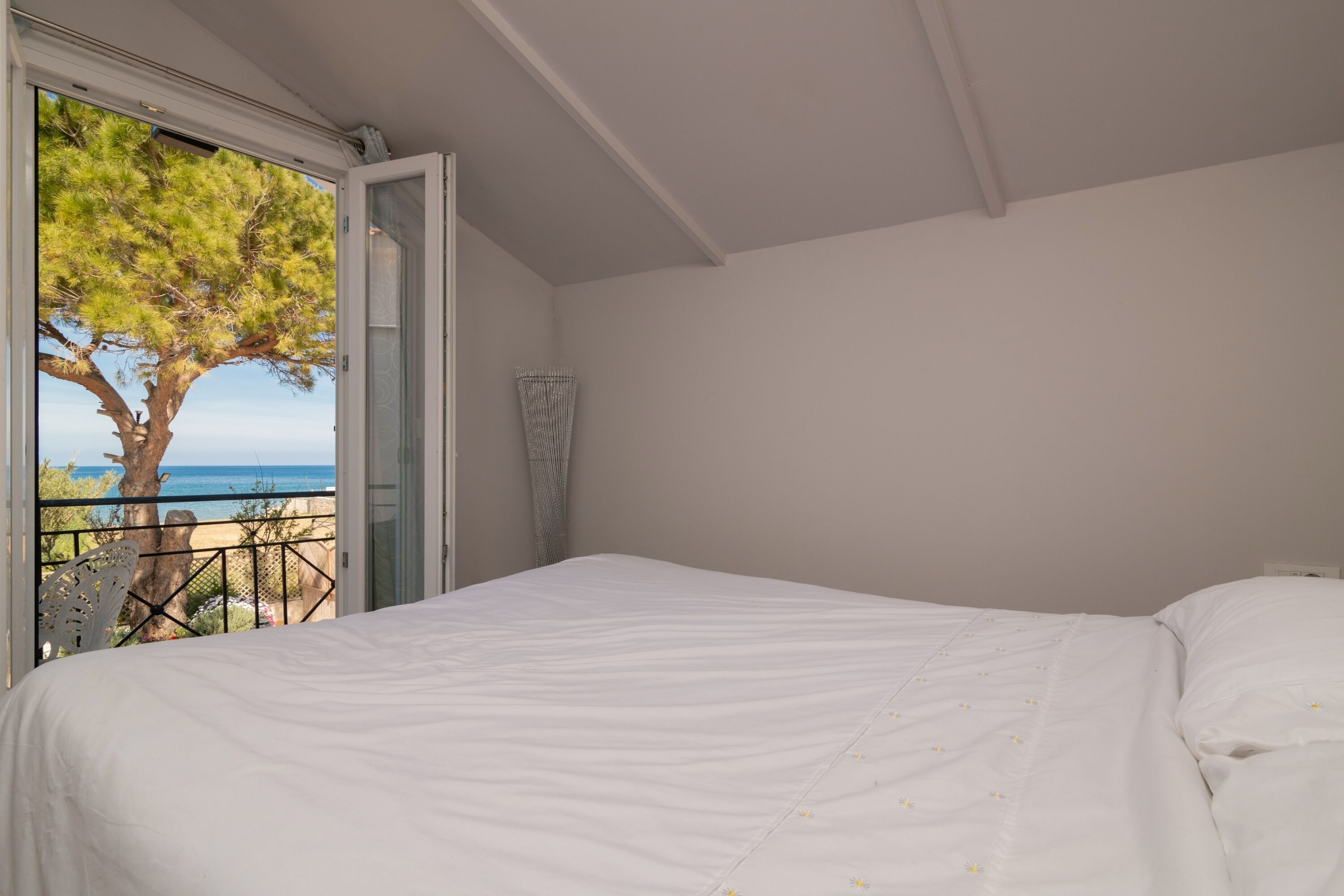Quarto com cama, janela com vista para o mar e varanda.
