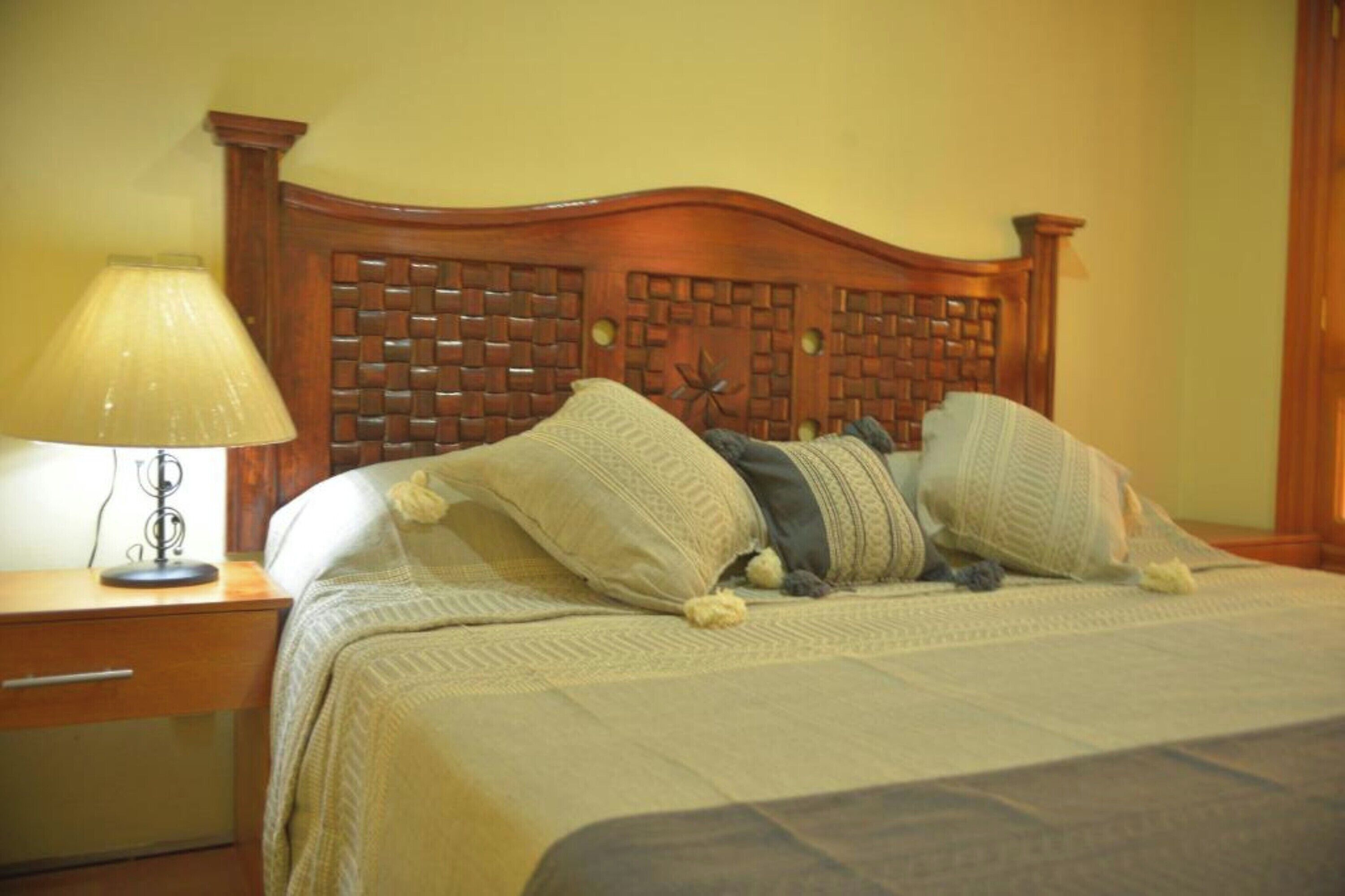 Uma cama com cabeceira de madeira, luminária de cabeceira e várias almofadas.
