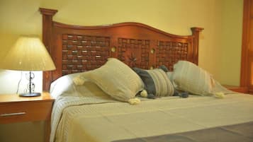 Uma cama com cabeceira de madeira, luminária de cabeceira e várias almofadas.