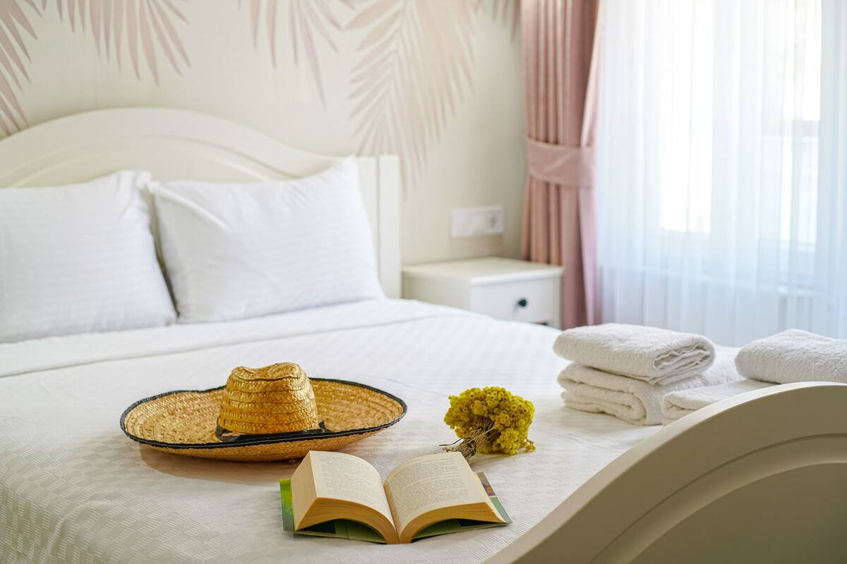 Cama bem arrumada com chapéu de palha, um livro e um buquê de flores amarelas.