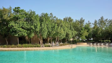 Piscina com água azul cristalina, rodeada por árvores e espreguiçadeiras.