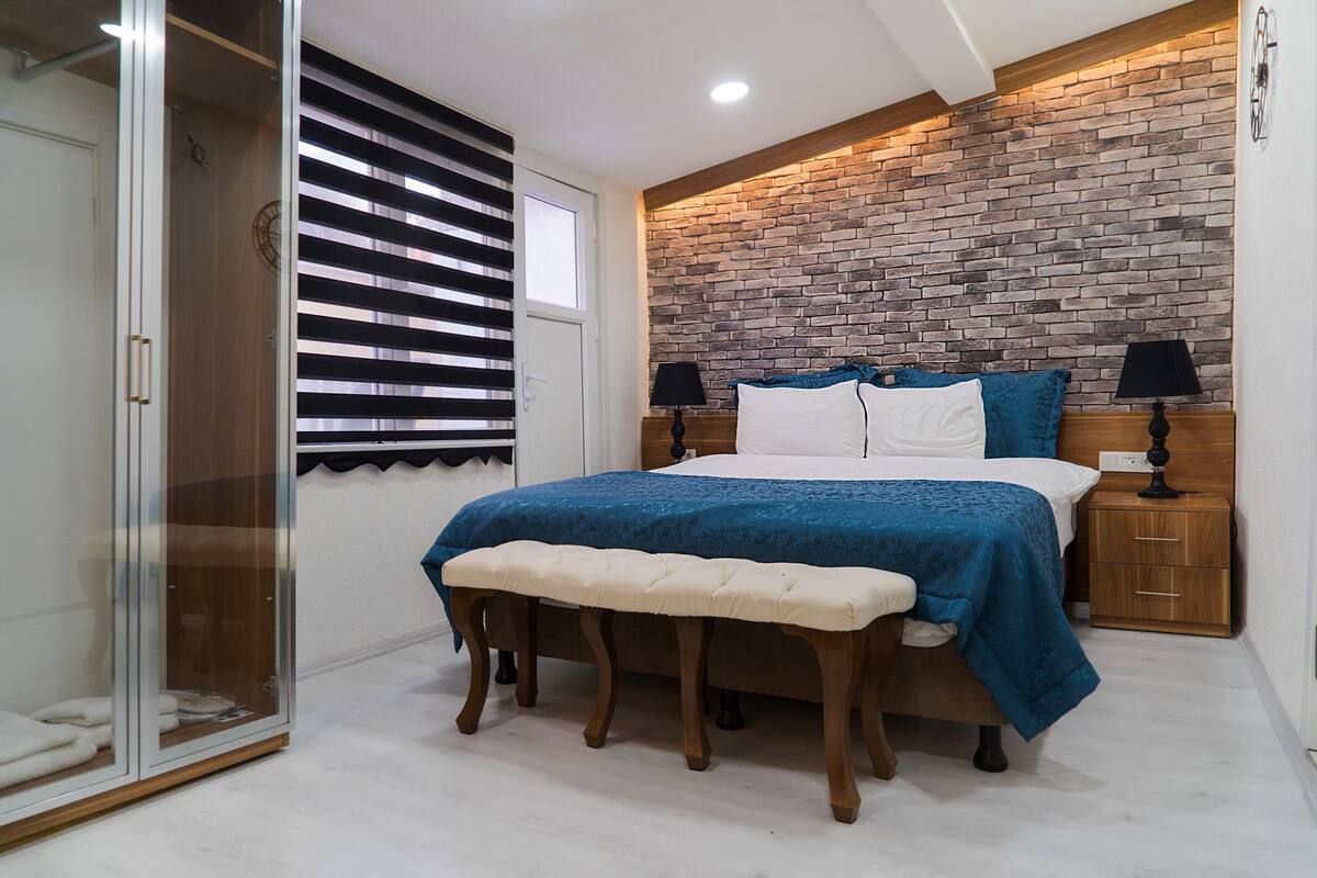 Quarto com cama, um banco, mesas de cabeceira e guarda-roupa.