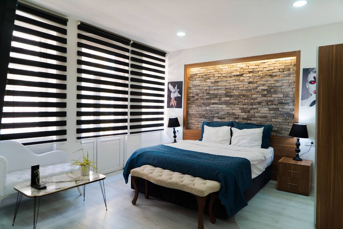Um quarto moderno com uma cama grande, um banco, uma mesa pequena e uma mesinha de cabeceira.