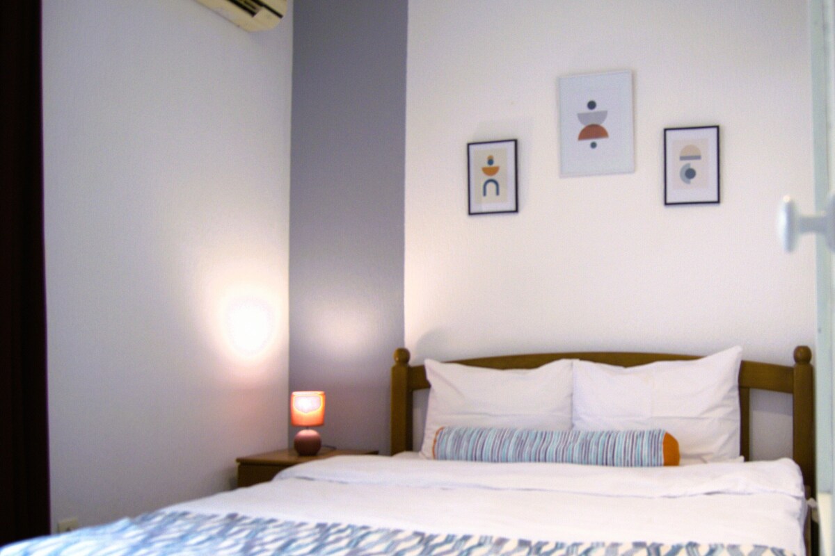 Uma cama com um edredom estampado, um abajur e duas molduras na parede.