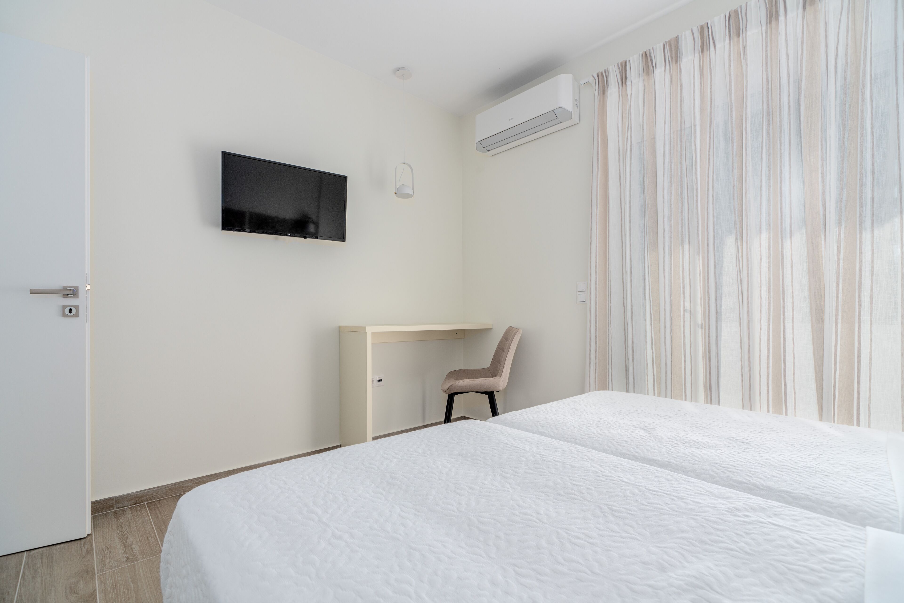 Quarto de hotel com cama, escrivaninha, cadeira, televisão e ar condicionado.