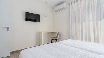 Quarto de hotel com cama, escrivaninha, cadeira, televisão e ar condicionado.