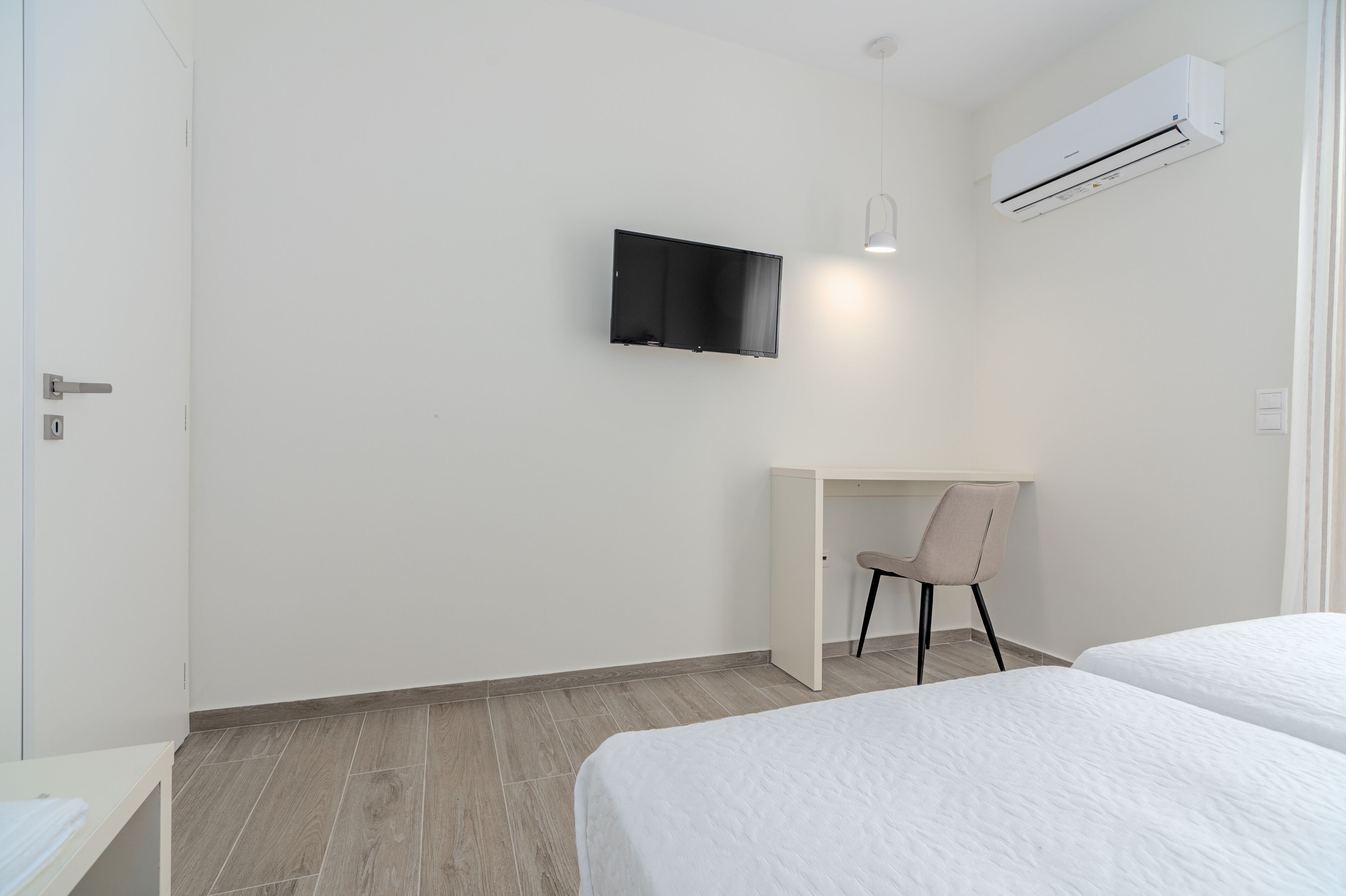 Quarto com cama, escrivaninha, cadeira, televisão e ar condicionado.