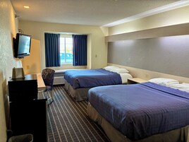Quarto de hotel com duas camas, uma televisão sobre uma escrivaninha e uma janela com cortinas.