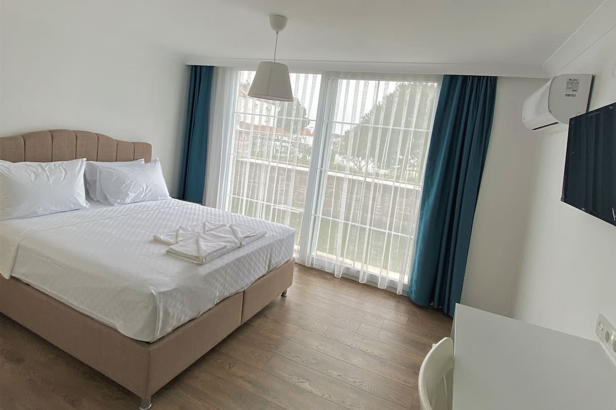 Quarto de hotel com cama, escrivaninha e janela com cortinas.