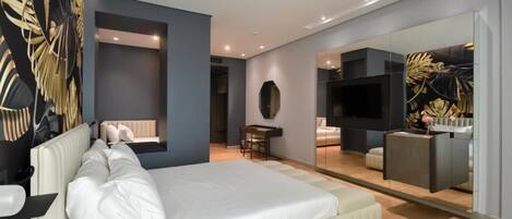 Quarto de hotel moderno com uma cama grande, uma escrivaninha, uma TV e um espaço de estar com vista para a cidade.