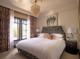 Uma cama grande com almofadas estampadas, um candelabro e um quadro acima.