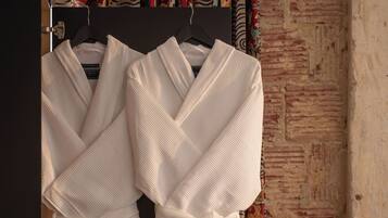 Dois robes brancos pendurados em um cabide contra uma parede de tijolos.