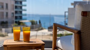 Uma mesa de madeira com dois copos de suco de laranja e uma cadeira de vime com almofada branca.