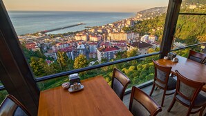 Espaço de refeições com mesa e cadeiras, com vista para a paisagem urbana costeira, incluindo edifícios e um cais.