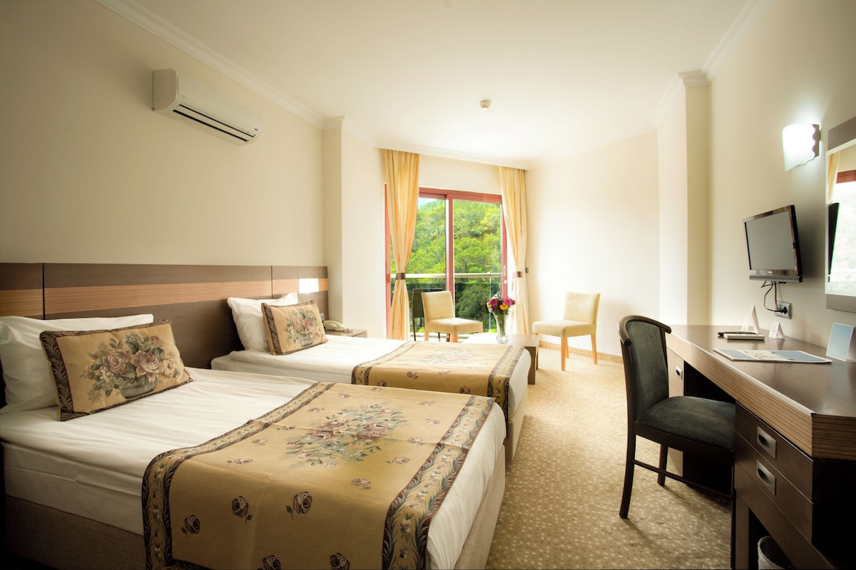Quarto de hotel com duas camas, uma escrivaninha, uma cadeira e uma televisão.