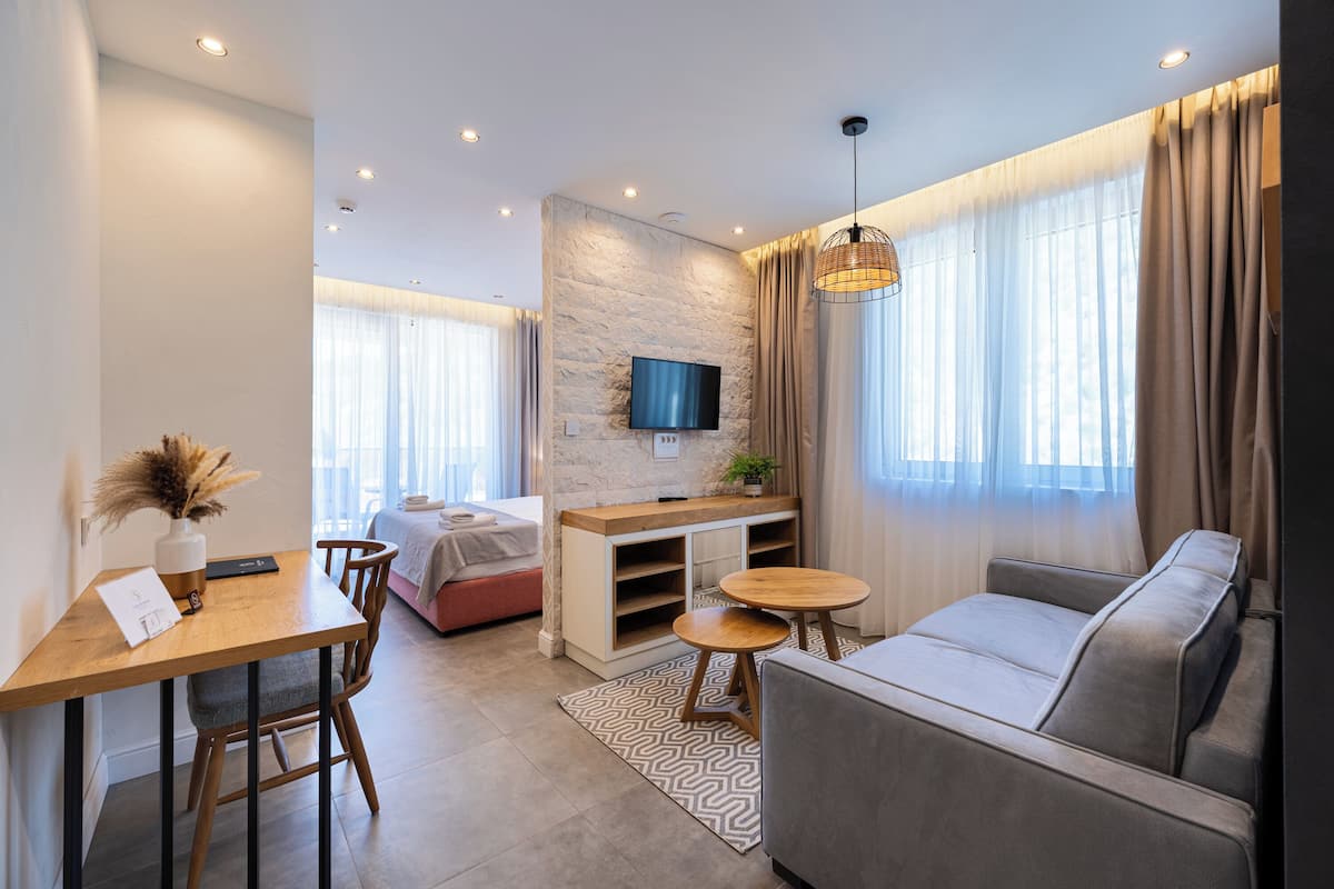 Uma sala de estar moderna com sofá, mesa de jantar, TV fixada em uma parede de pedra e uma janela grande com cortinas.