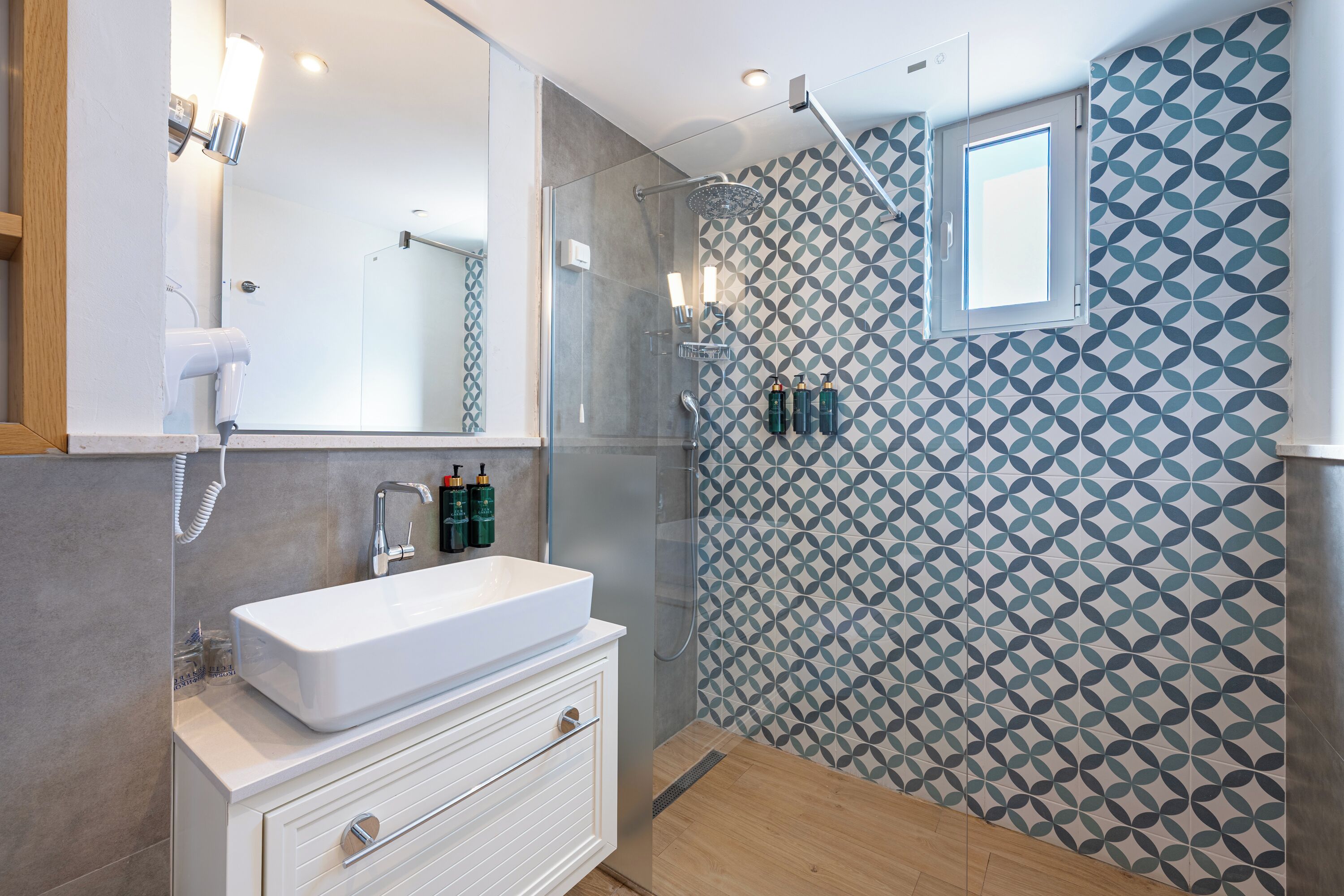 Uma casa de banho moderna com um espelho grande, uma sanita branca, um chuveiro e azulejos com padrão nas paredes.