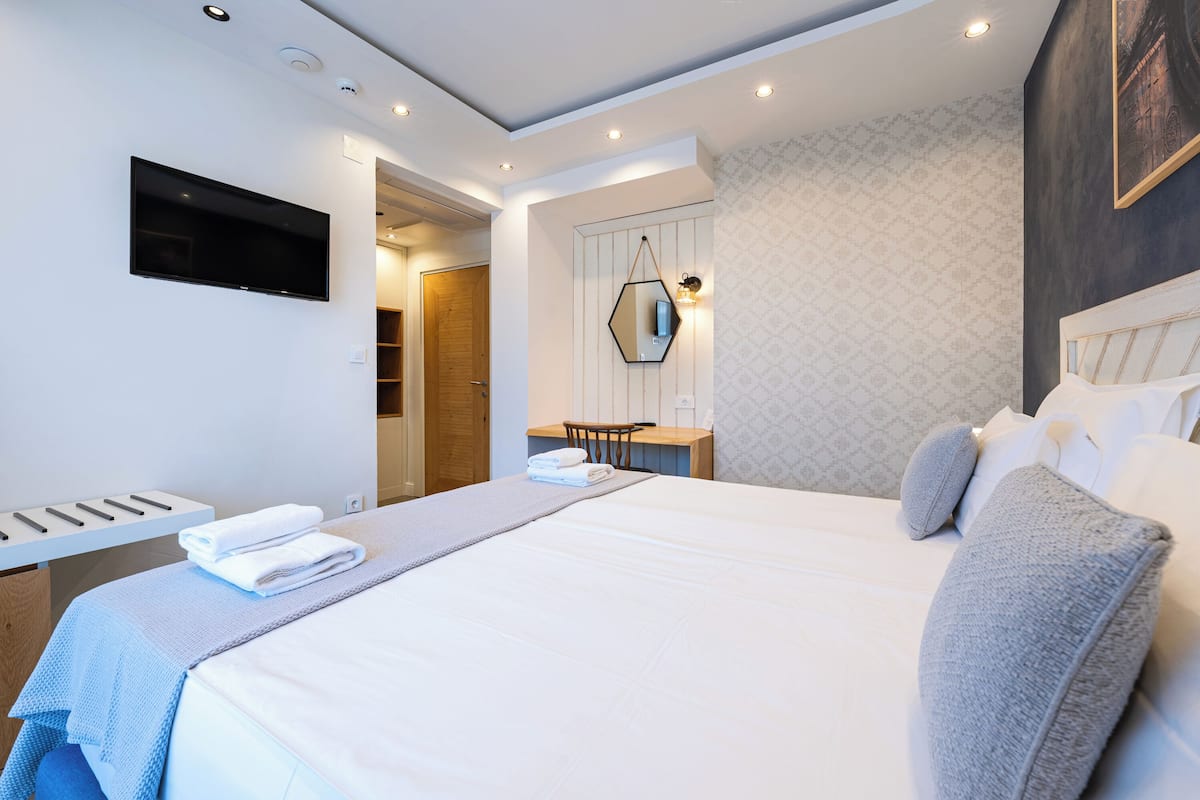 Quarto de hotel moderno com uma cama grande, uma televisão de tela plana, uma escrivaninha com cadeira e um espelho.