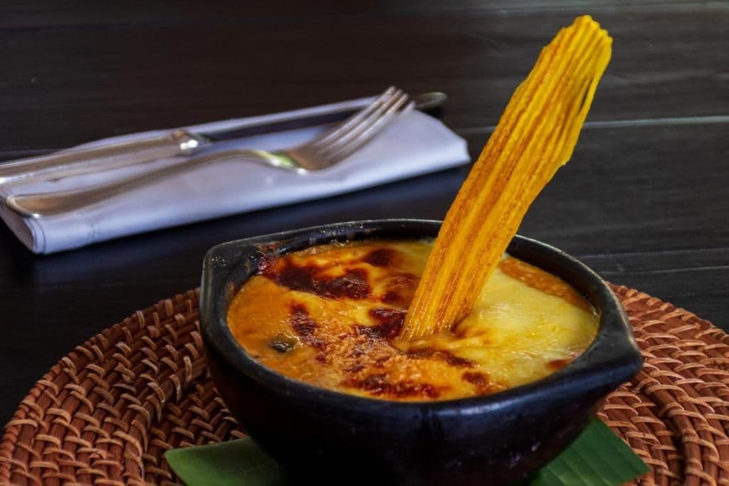 Uma tigela de comida com uma colher sobre um tapete trançado.