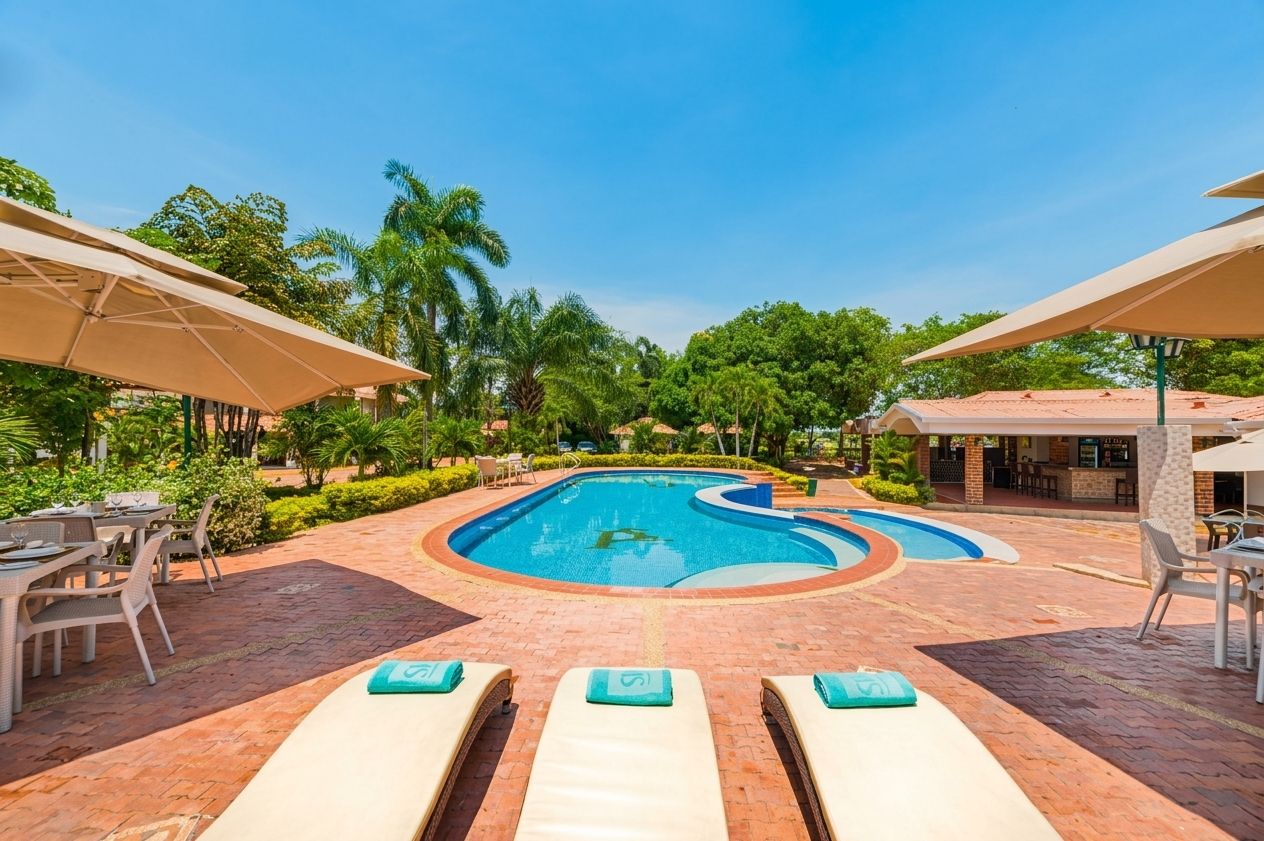 Piscina com espreguiçadeiras e guarda-sóis, rodeada por vegetação e um caminho de tijolos.