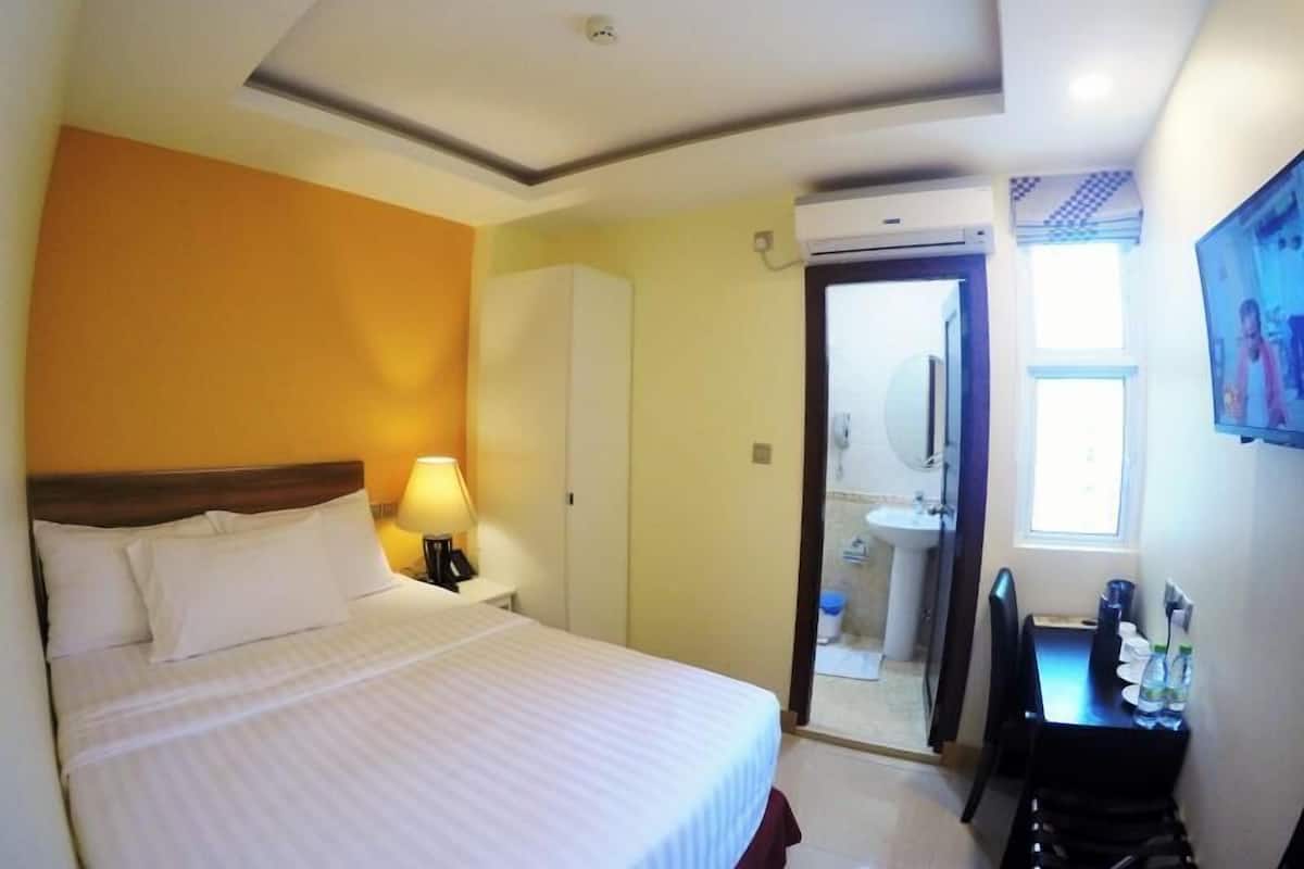 Quarto de hotel com cama, escrivaninha, cadeira, televisão e banheiro visível por uma porta aberta.