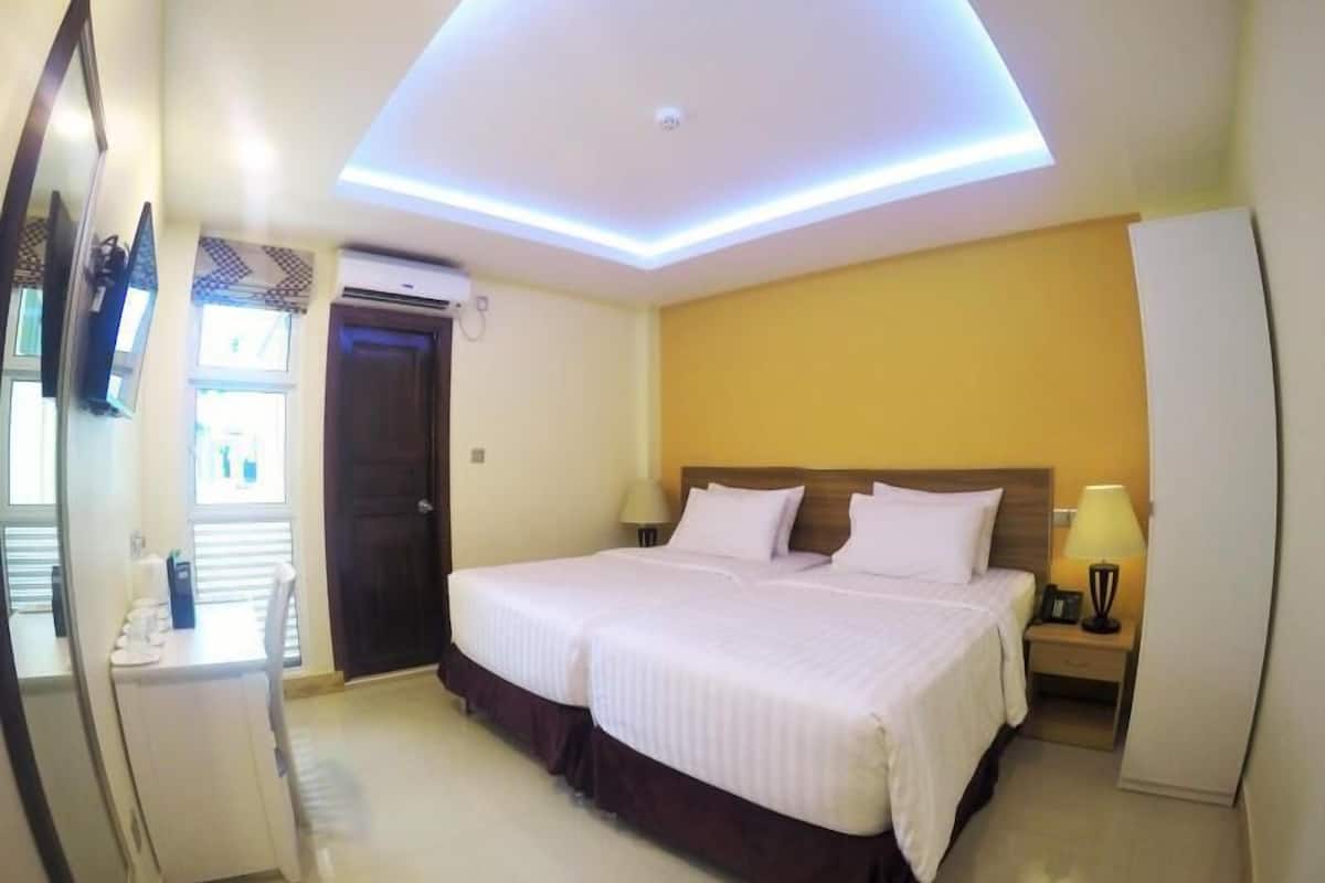 Quarto de hotel com cama de casal, mesas de cabeceira, escrivaninha e janela com persianas.